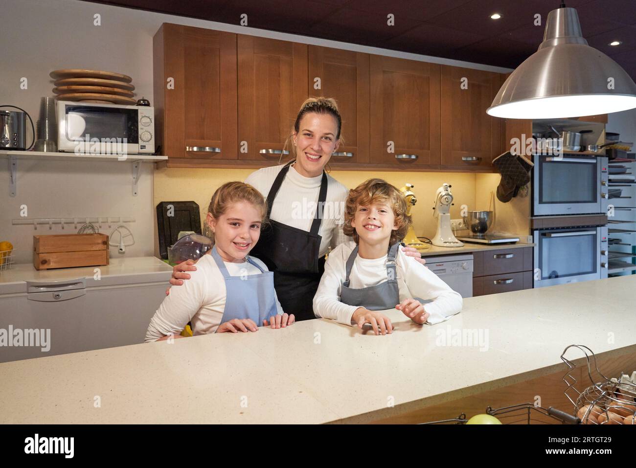 Brother and sister hugged by smiling woman wearing aprons standing at ...