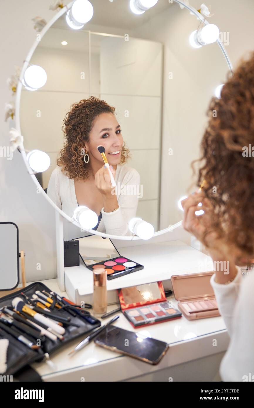 Mirror reflection of young smiling woman doing makeup of cheeks with ...