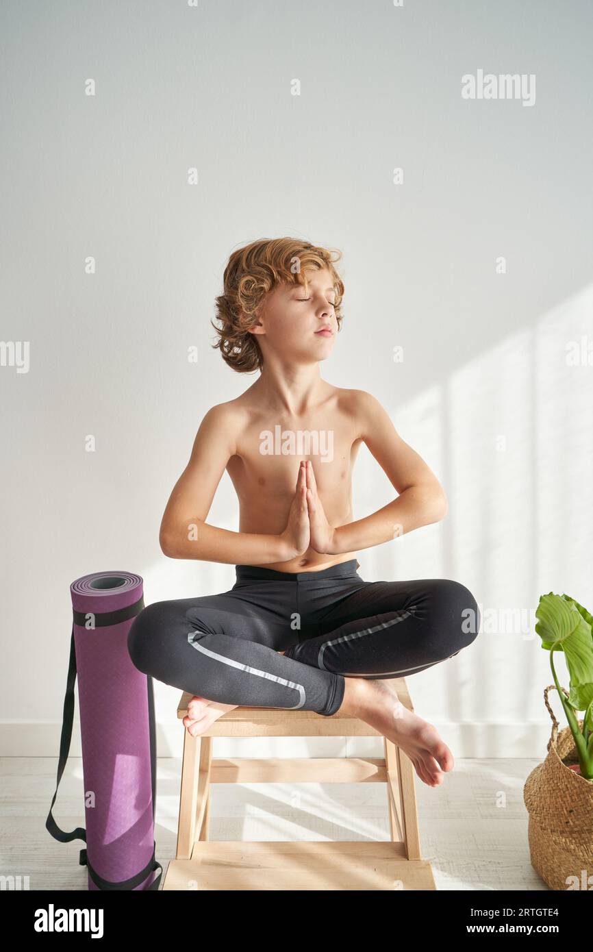 Full body of barefoot preteen boy sitting in Padmasana pose with ...