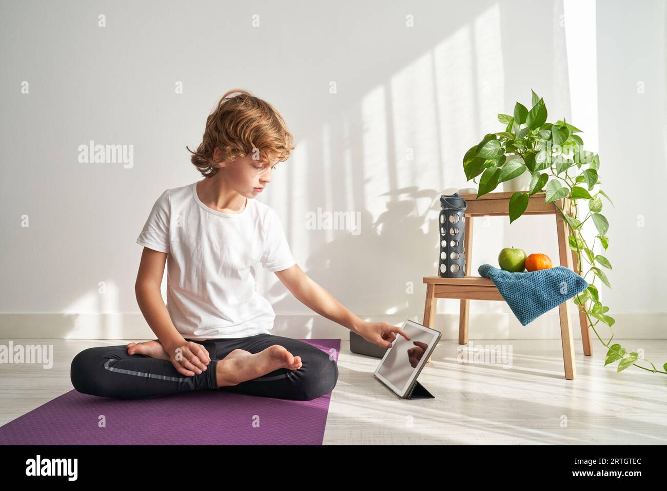 Full body of barefoot blond curly haired boy sitting in Padmasana asana ...