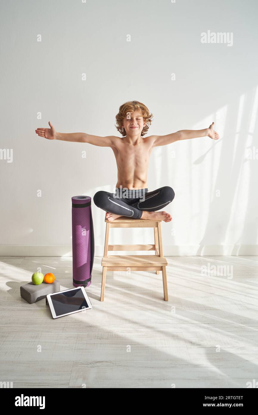 Full body of adorable boy concentrating in Lotus pose with spread arms ...