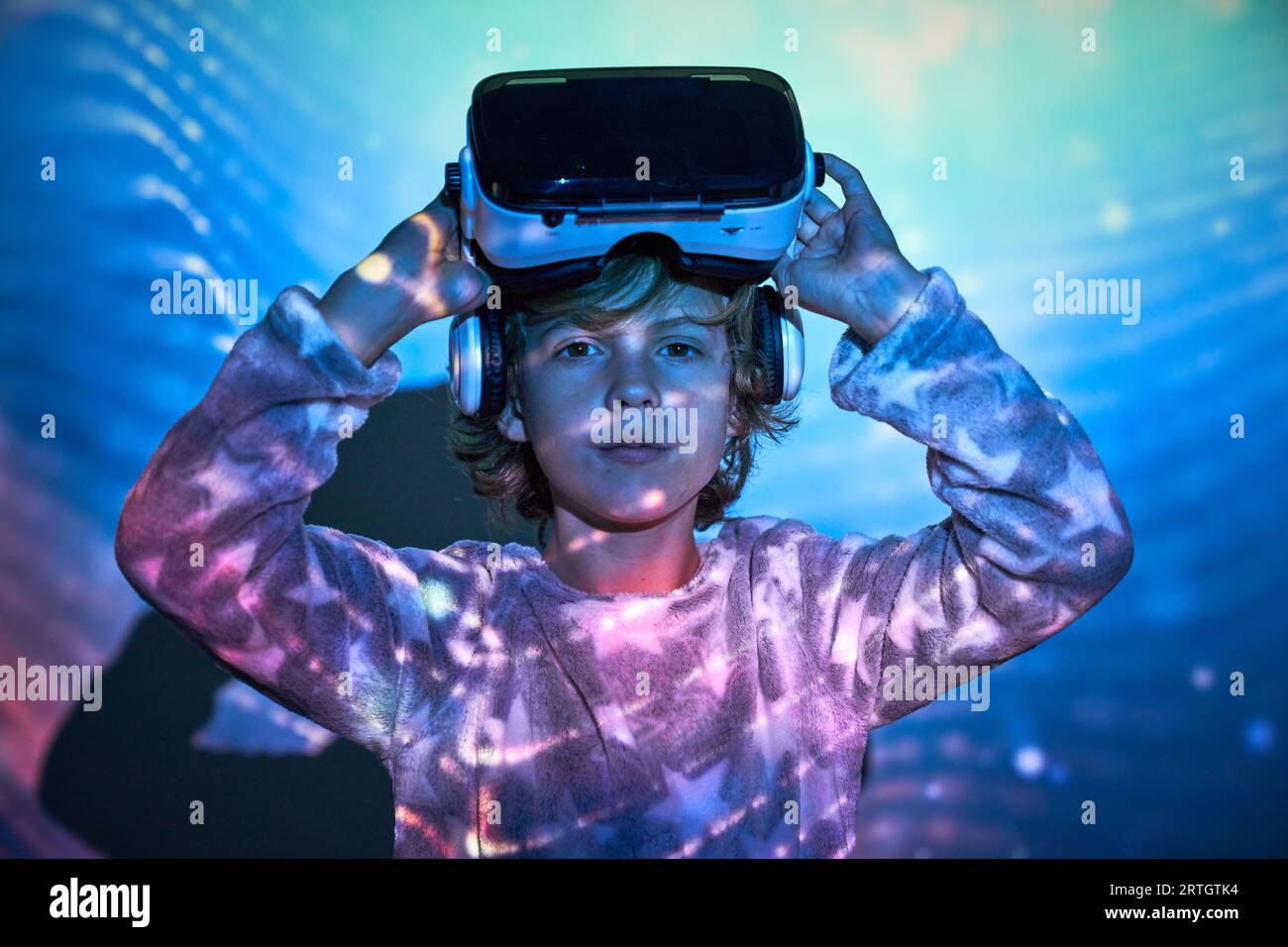 Cute little boy with blond hair in plush pajama taking of VR headset ...