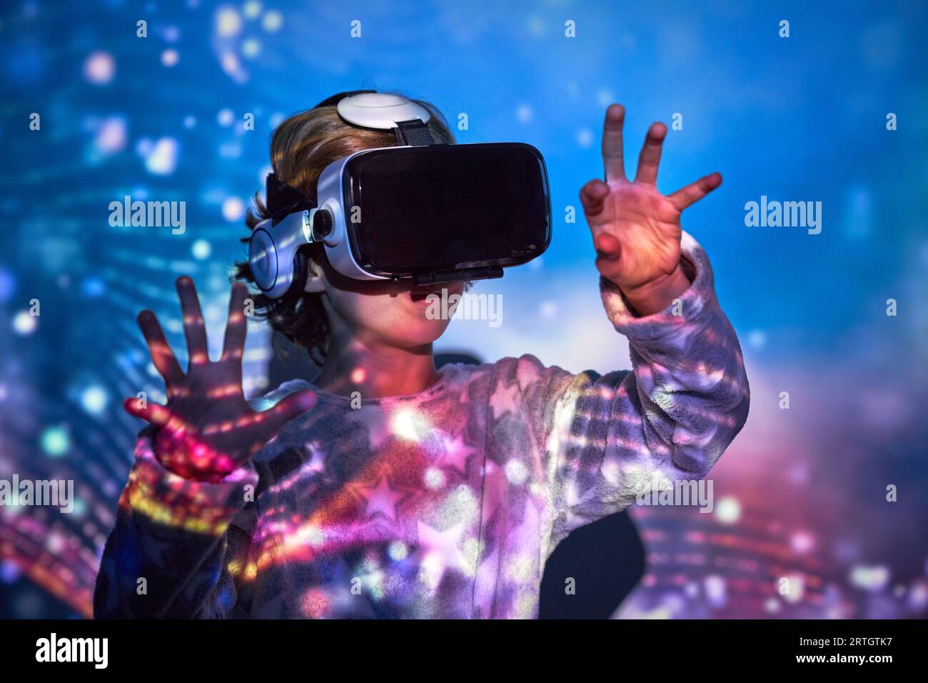 Curious little boy with blond hair in warm pajama and VR headset ...