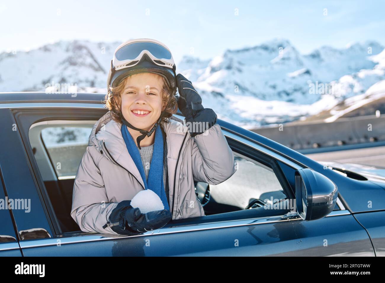 Positive boy in ski goggles looking away while leaning out car window ...