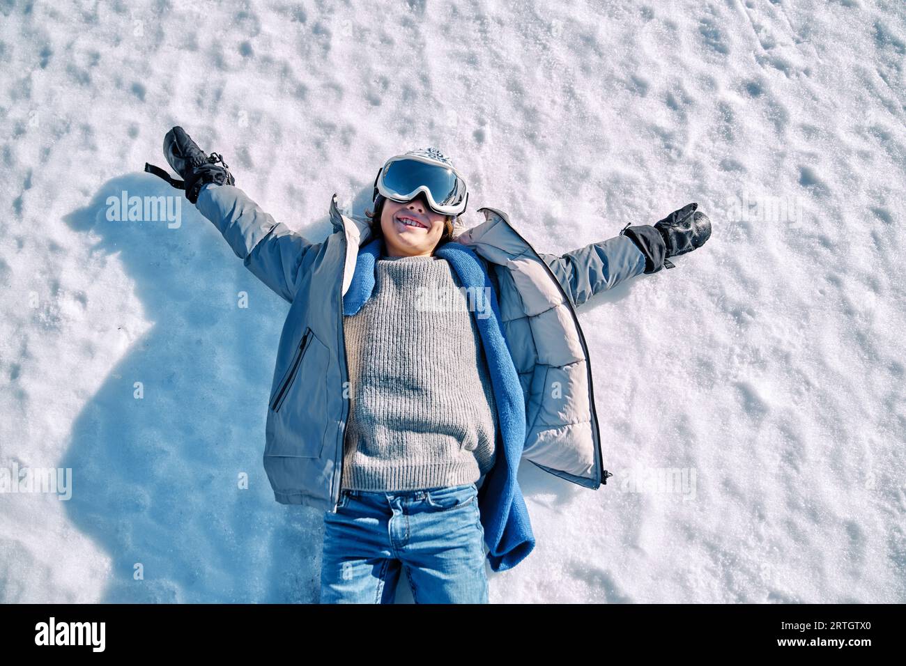 From above of happy kid wearing warm clothes and ski goggles resting on ...