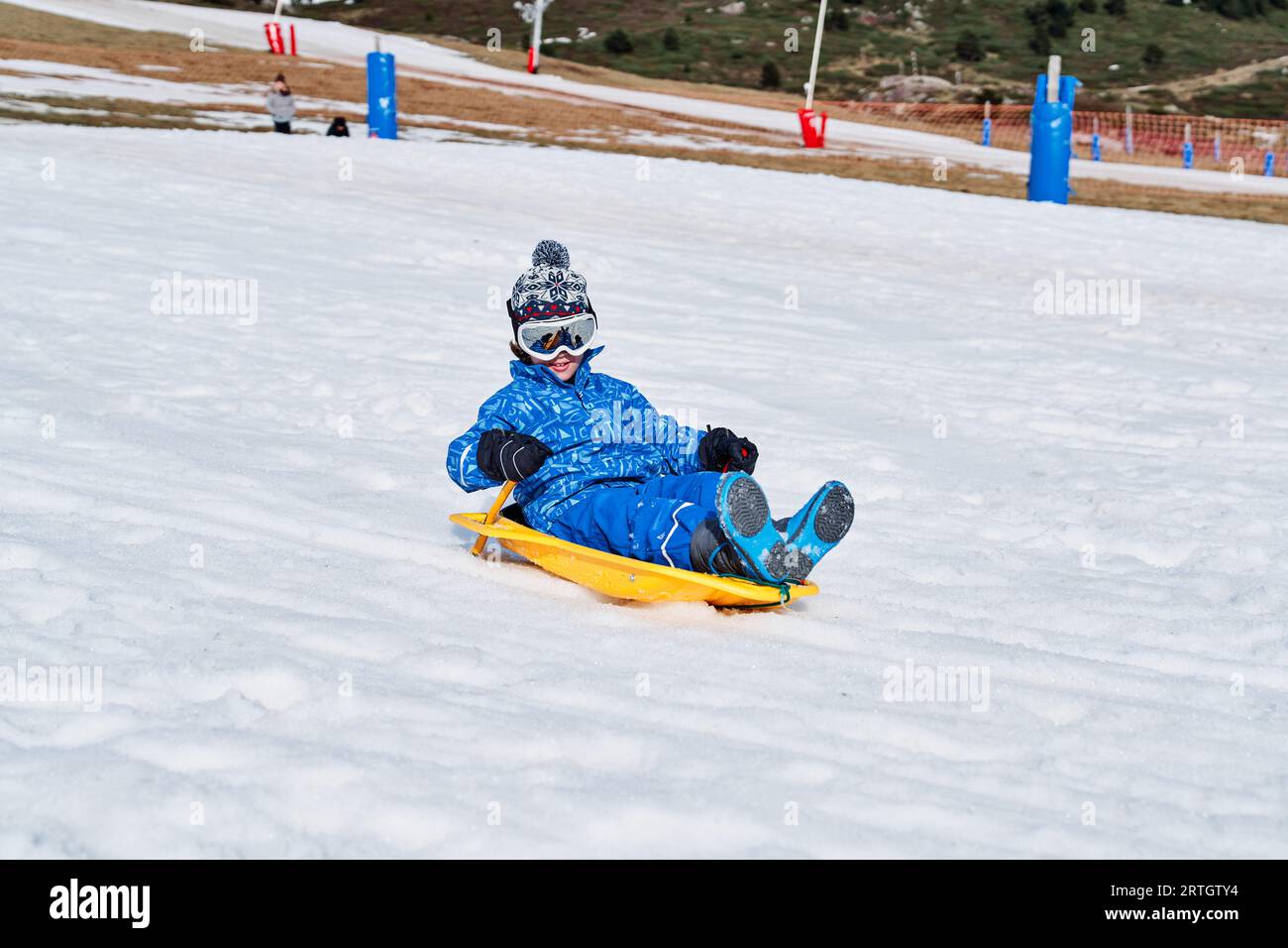 Kid in outerwear with hat and goggles controlling plastic sledge while ...