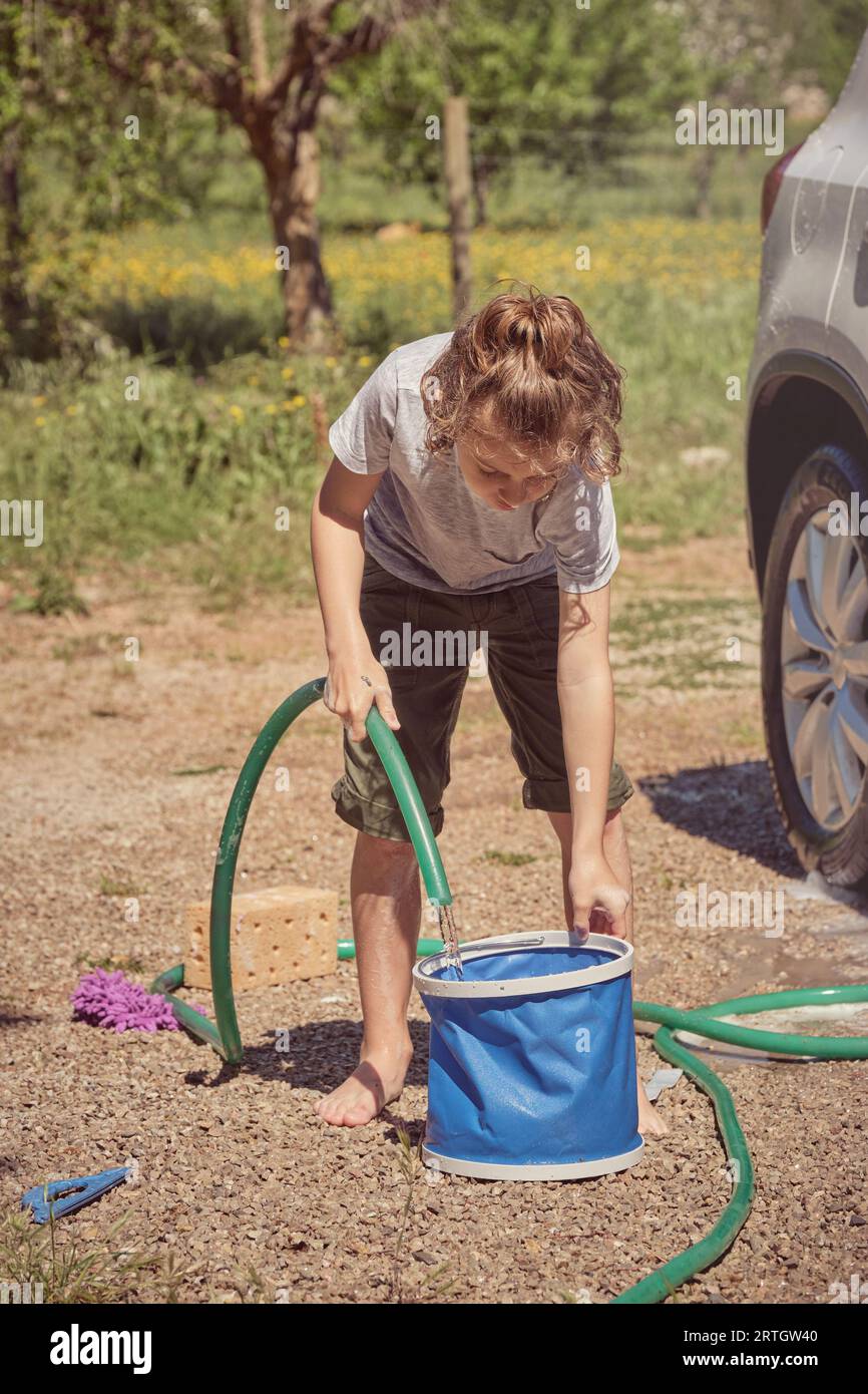 Full length of little kid pouring water in bucket with pipe while ...