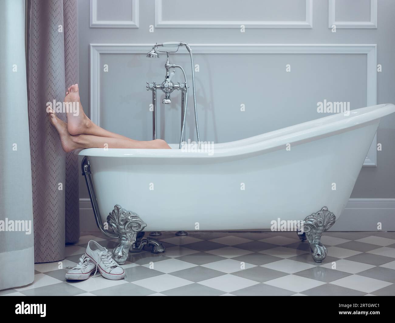 Unrecognizable barefoot female lying in white bathtub with legs out and ...