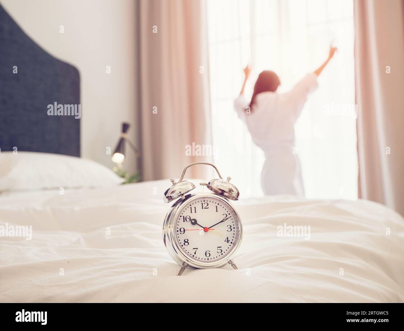 Back view of unrecognizable female standing near window and bed with ...