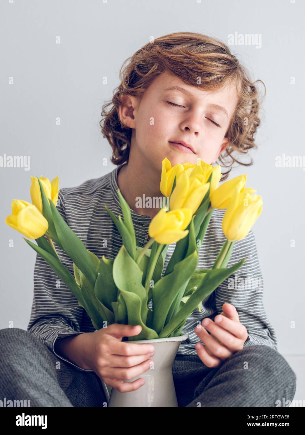 Adorable kid smelling bunch of yellow tulip flowers in vase and ...