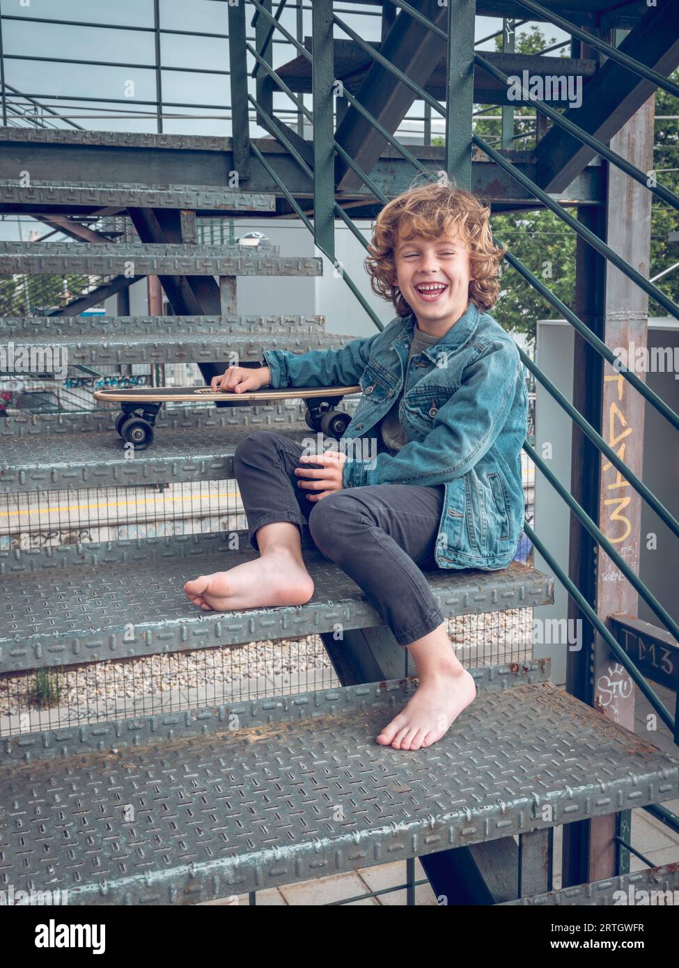 From below of full body of barefoot happy preteen boy sitting on steps ...