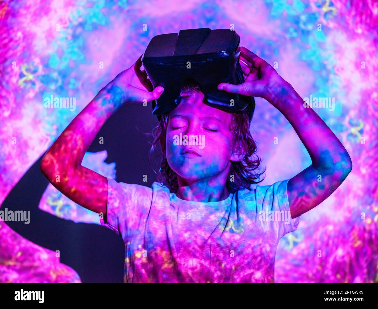 Kid with closed eyes taking VR headset off after exploring cyberspace ...