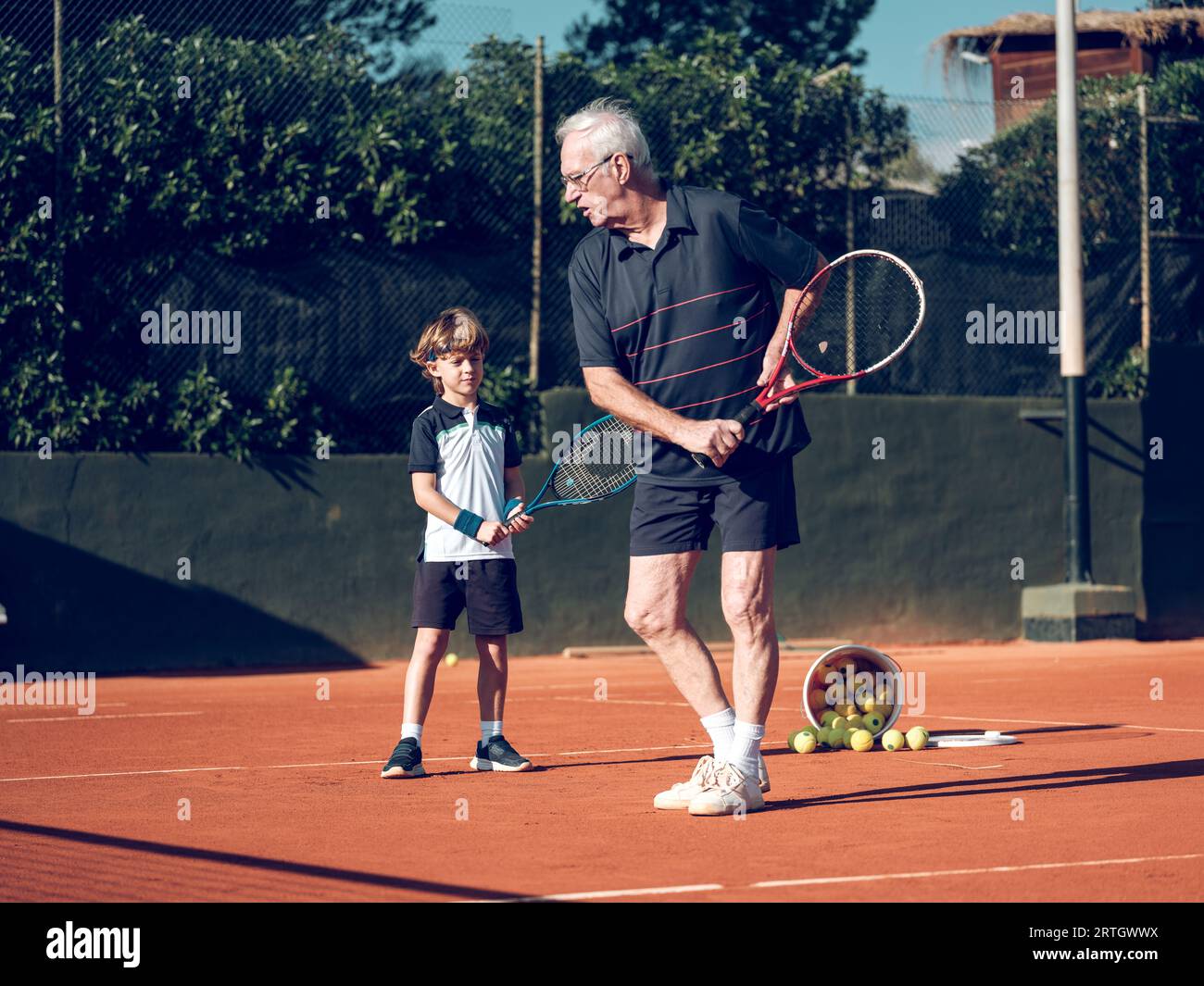 Side view of full body elderly coach demonstrating tennis technique ...