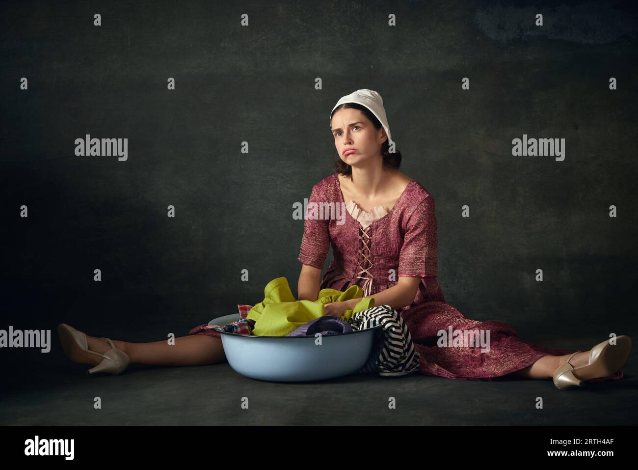 Young tired woman in costume of medieval maid sitting on floor with ...