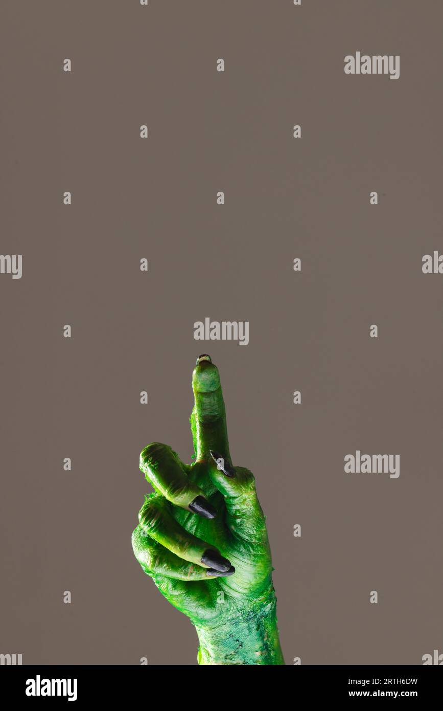 Vertical image of green monster hand with black nails pointing with ...