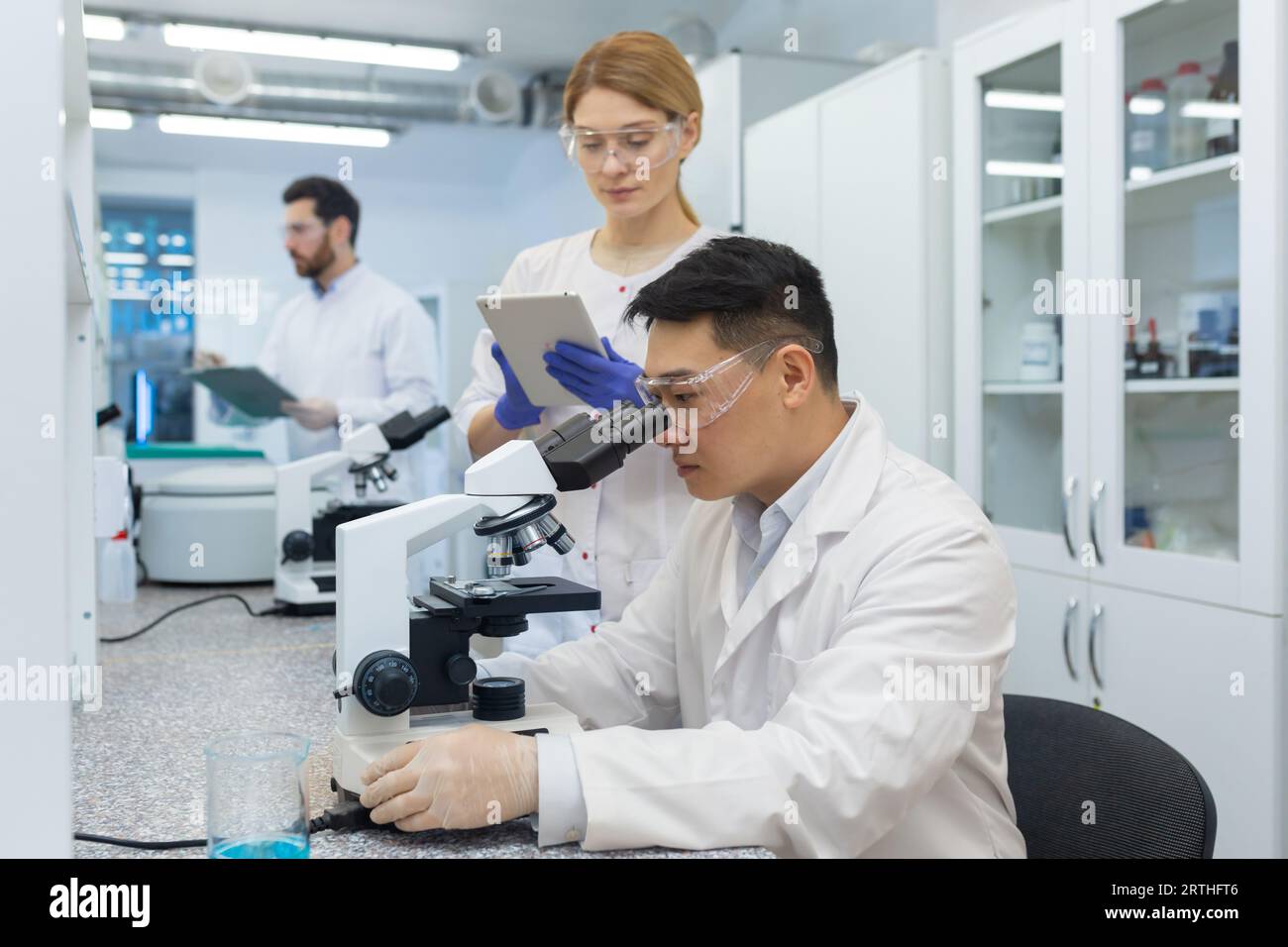 Asian young man working in laboratory together with colleagues. Sits at ...