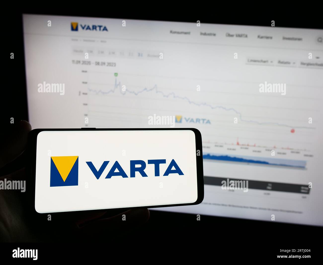 Person holding mobile phone with logo of German battery company Varta AG on screen in front of ...