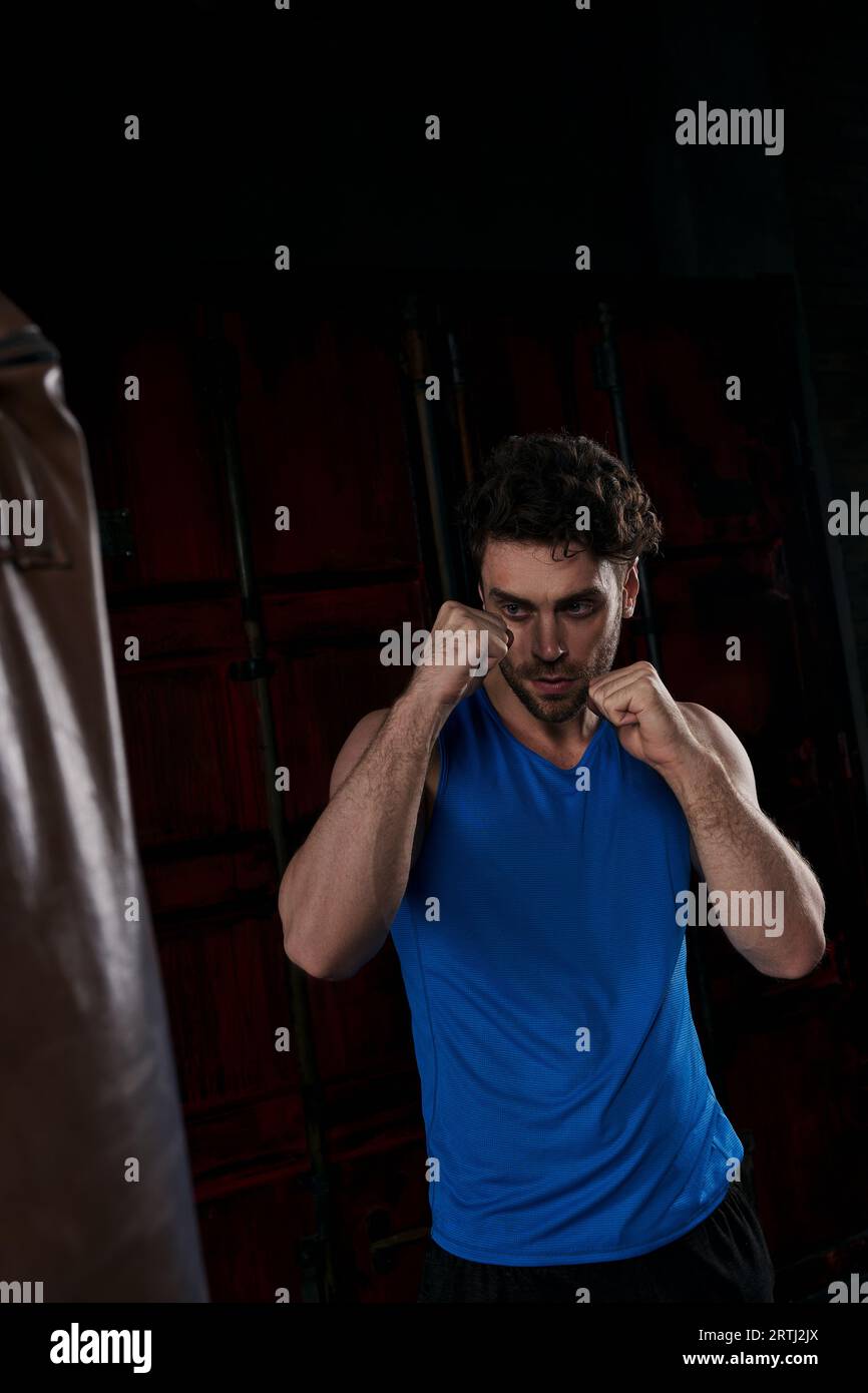 strong man in blue tank top boxing punching bag at night in city ...