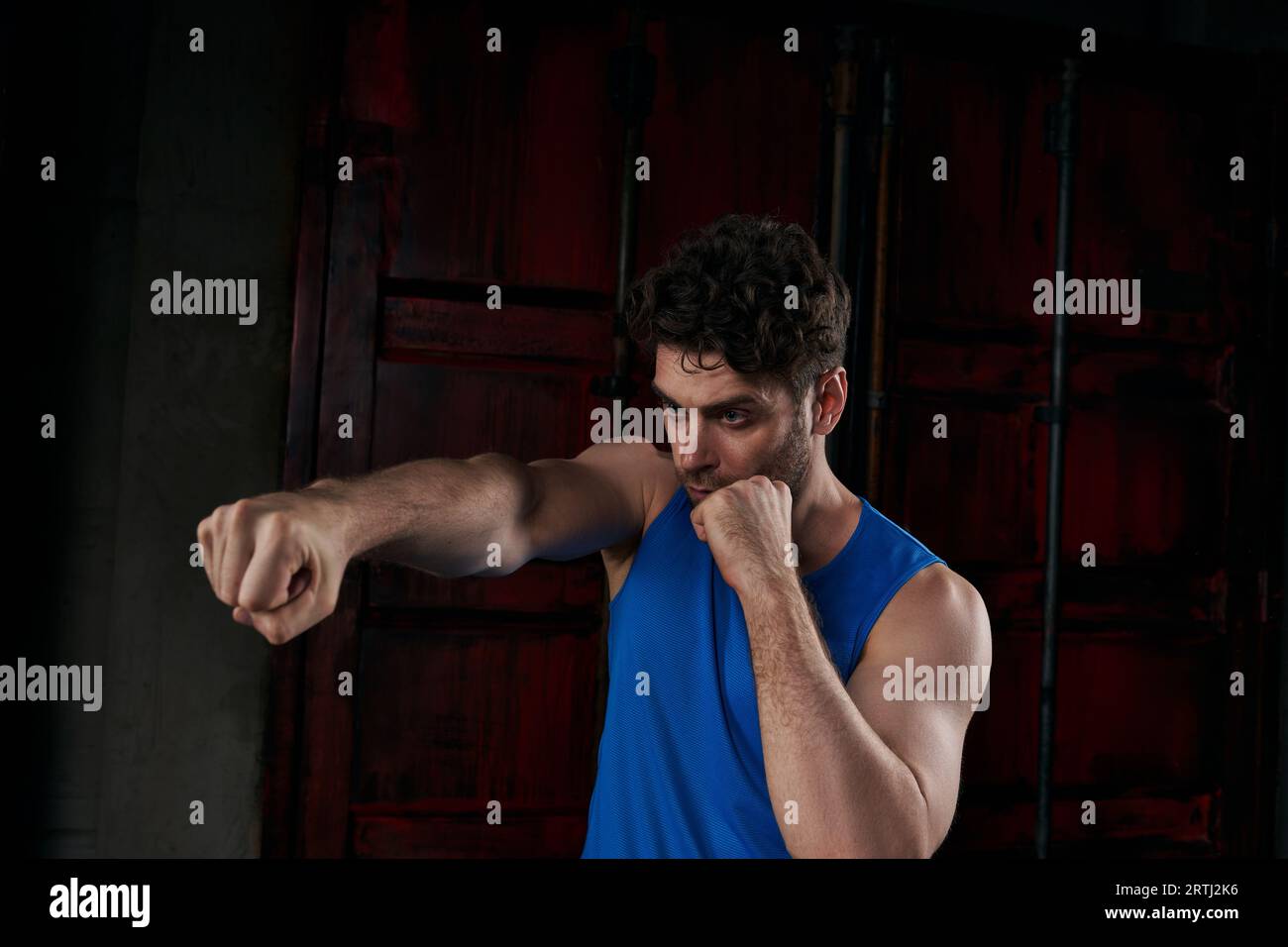 concentrated unshaven man working out and boxing in darkness on city ...