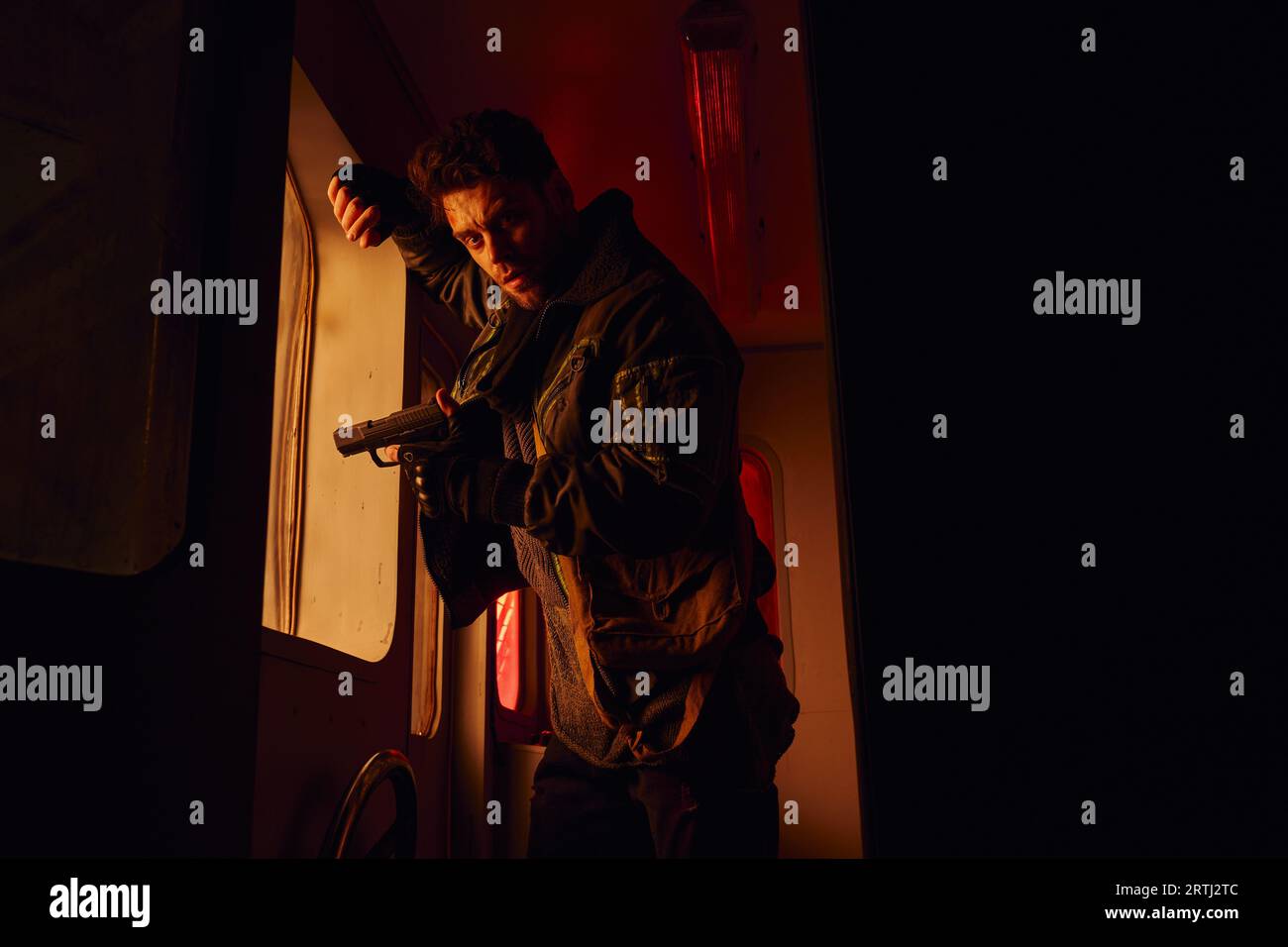 gloomy man with gun looking at camera in devastated subway carriage ...