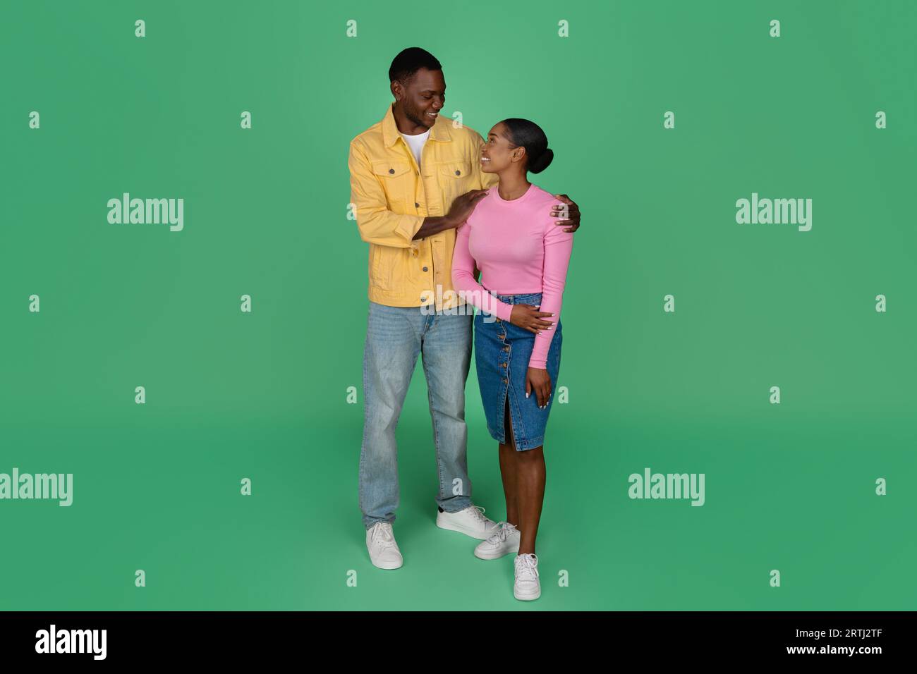 Happy beautiful millennial black couple cuddling on green background ...