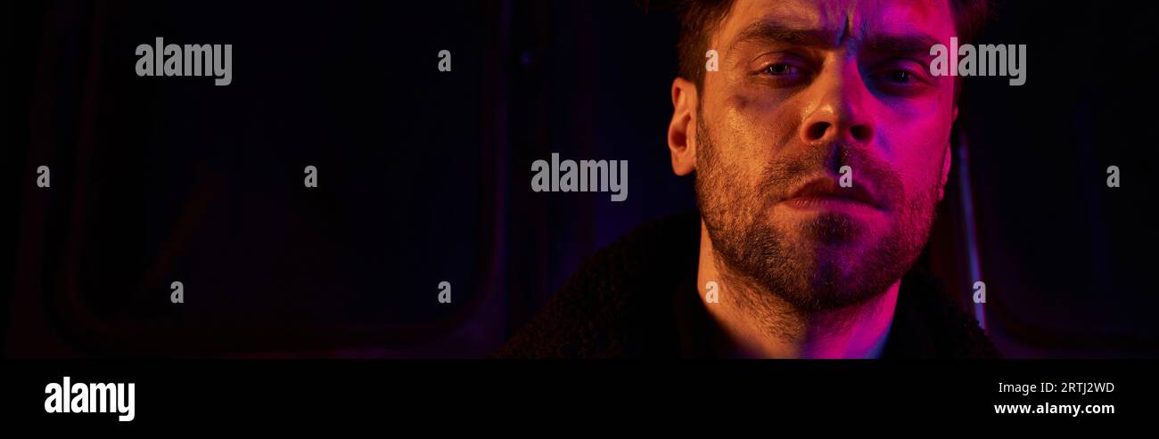 man with unshaven injured face looking at camera in red light of post ...