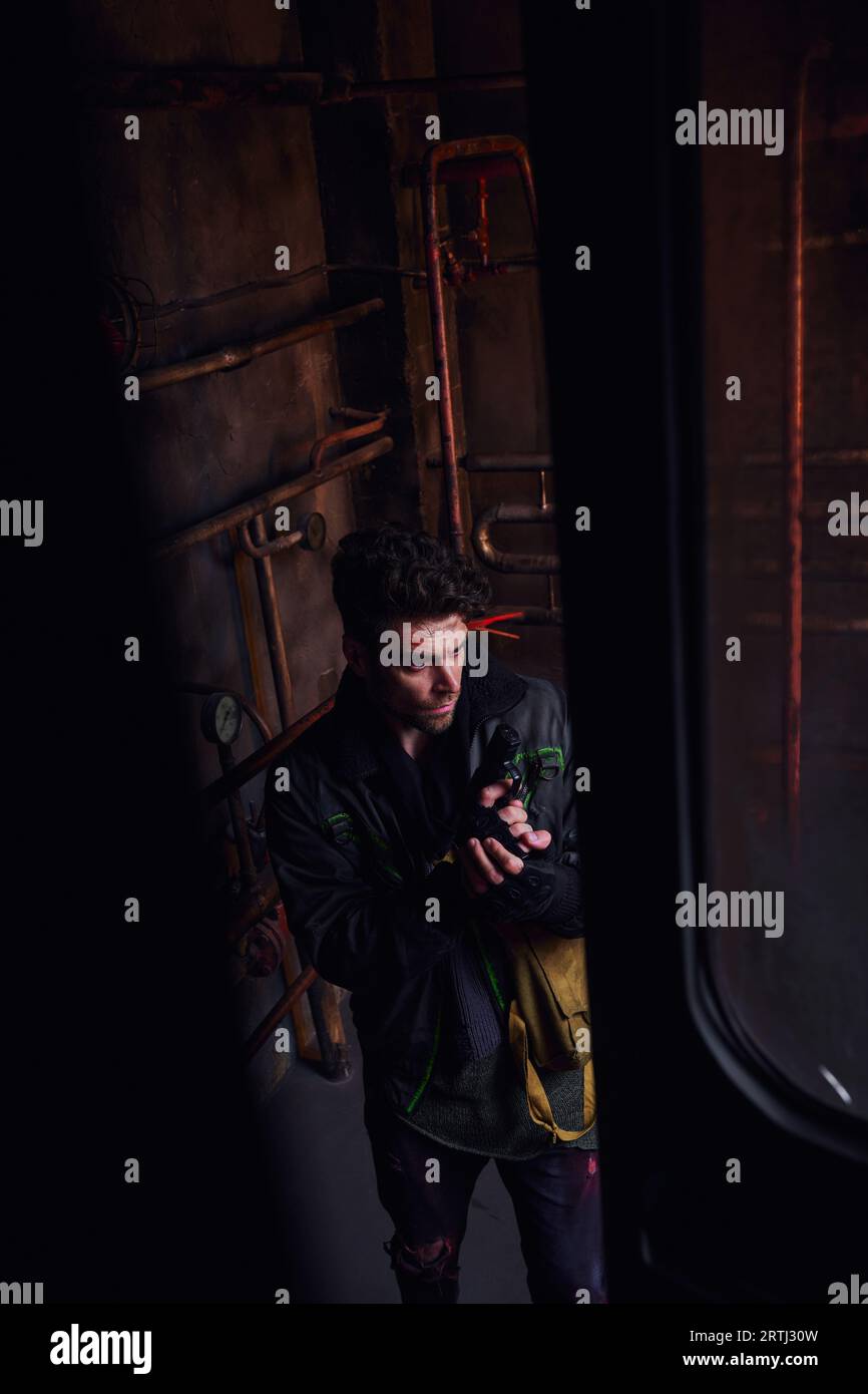 high angle view of man in worn clothes standing with gun in post ...