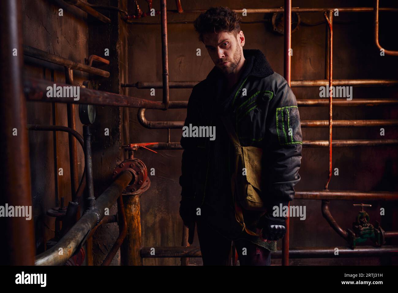 hopeless man in dirty clothes near rusty pipelines in underground ...