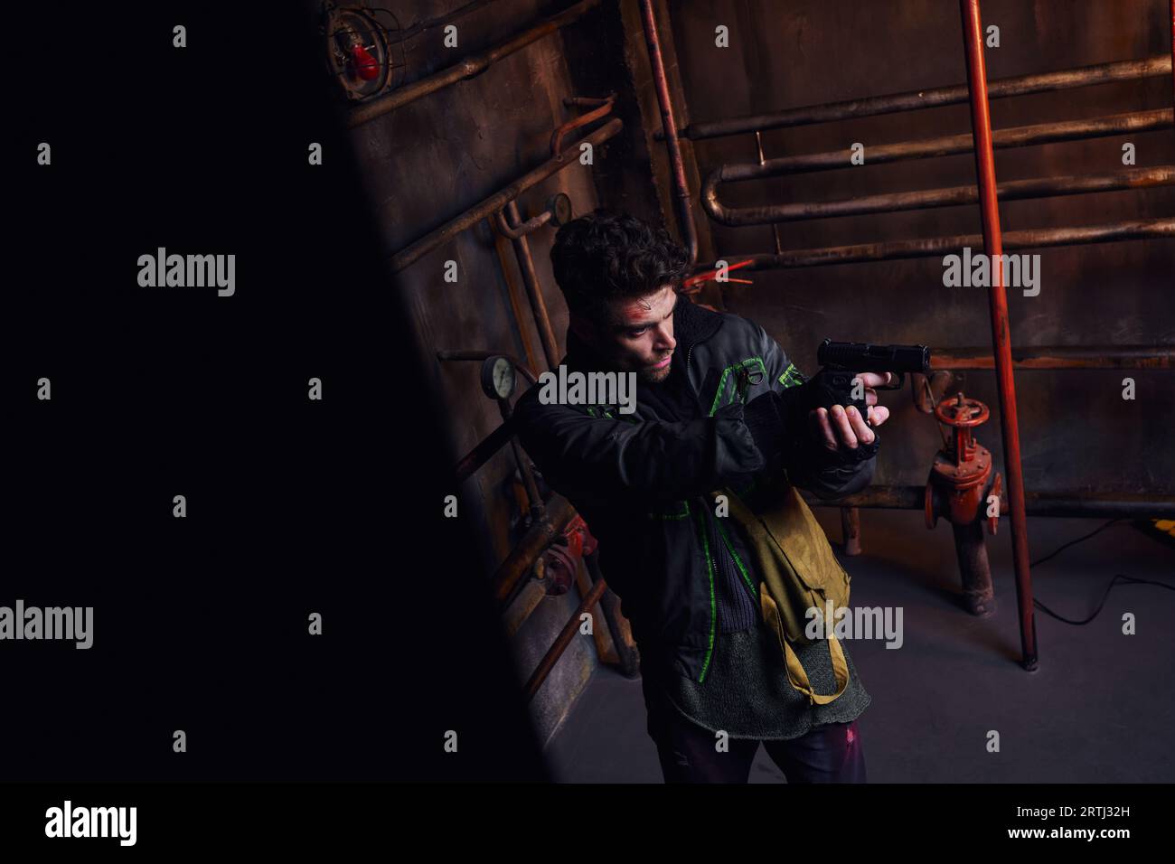 focused man aiming with gun in abandoned subway near rusty pipelines ...