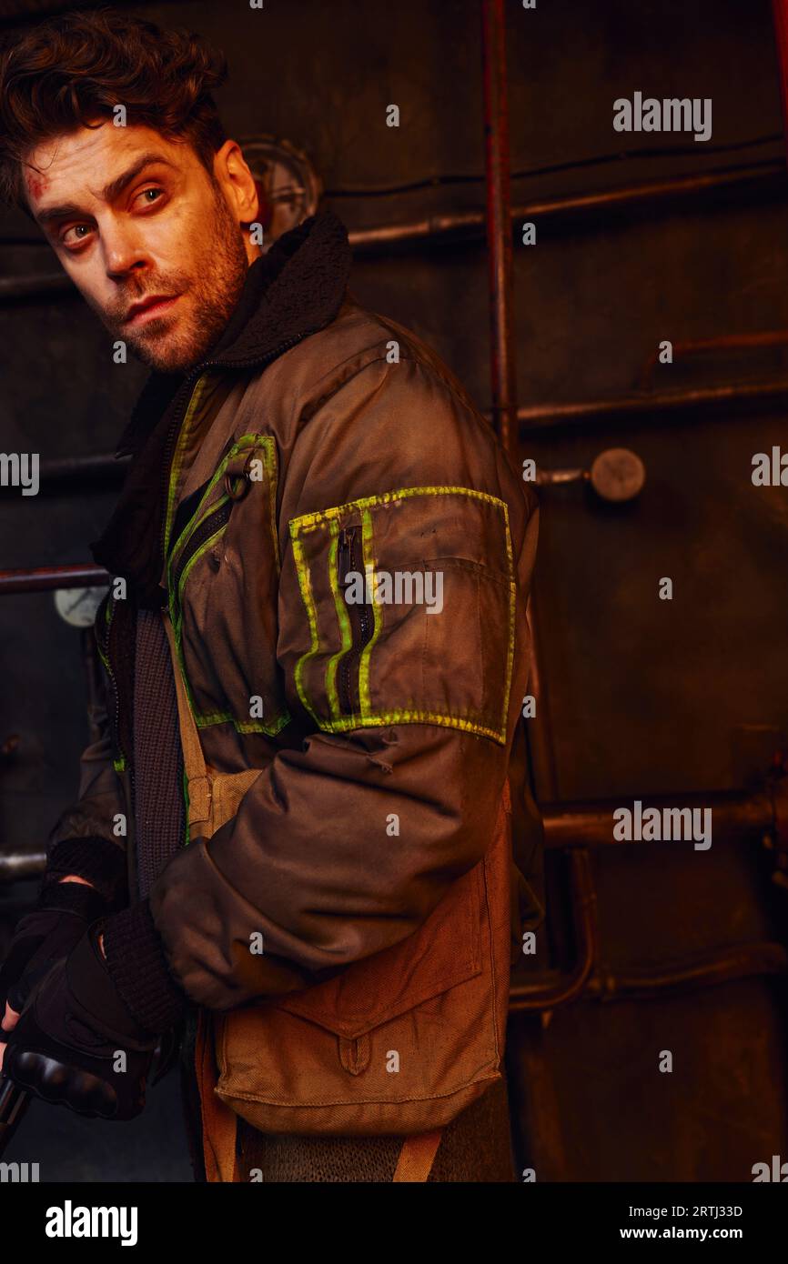 unshaven man in worn jacket looking away in red light of post-disaster ...
