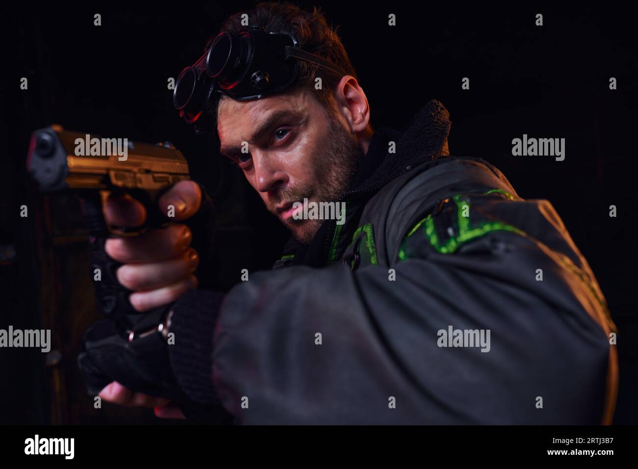 unshaven man with military googles aiming with gun in abandoned subway ...
