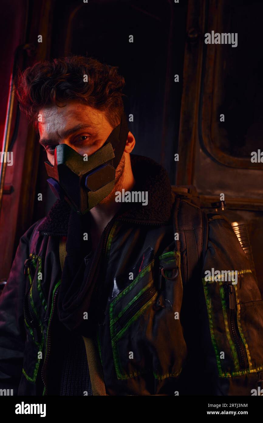 man in worn clothes and gas mask looking at camera in abandoned post ...