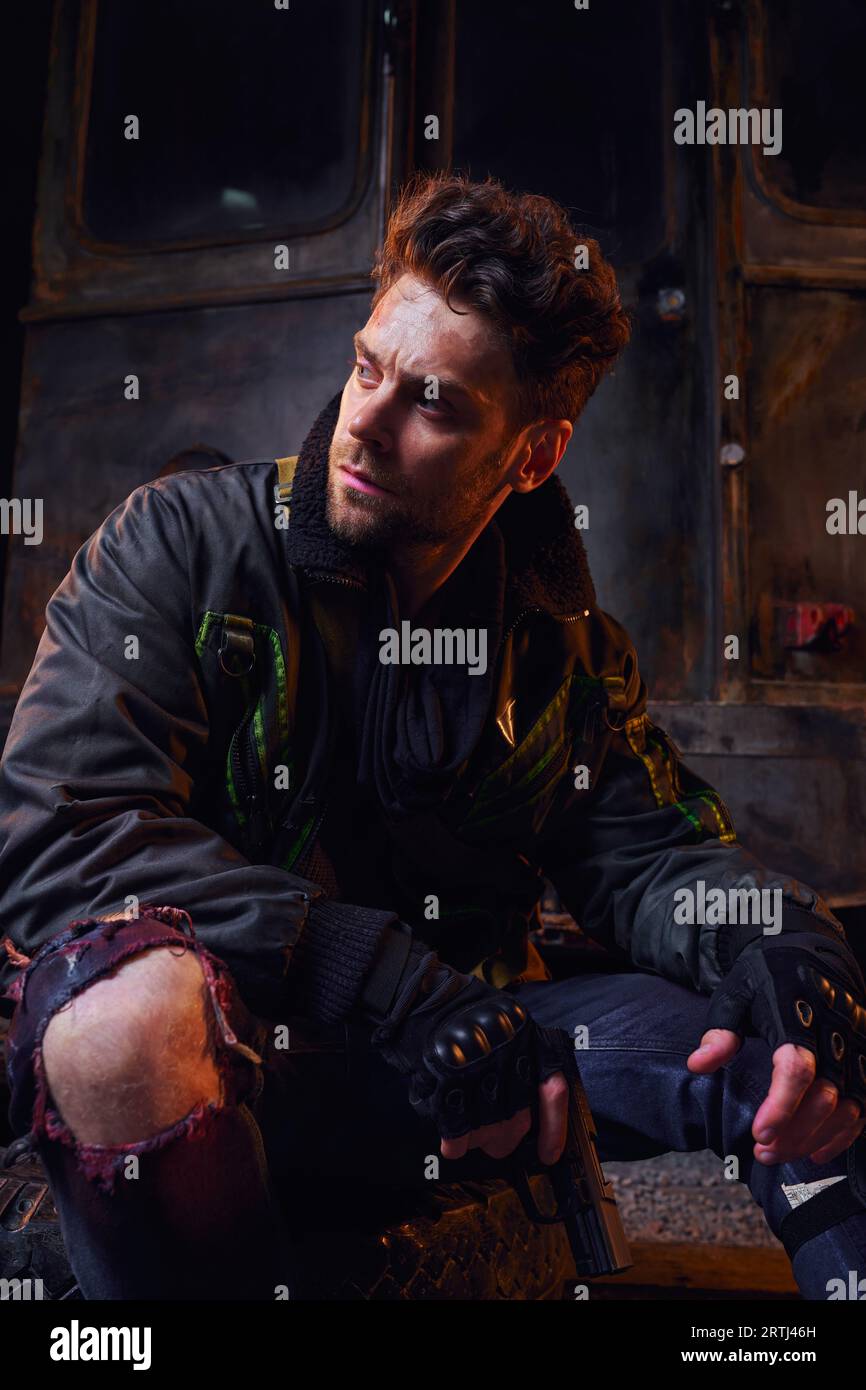 man with scratched unshaven face sitting and looking away in darkness ...