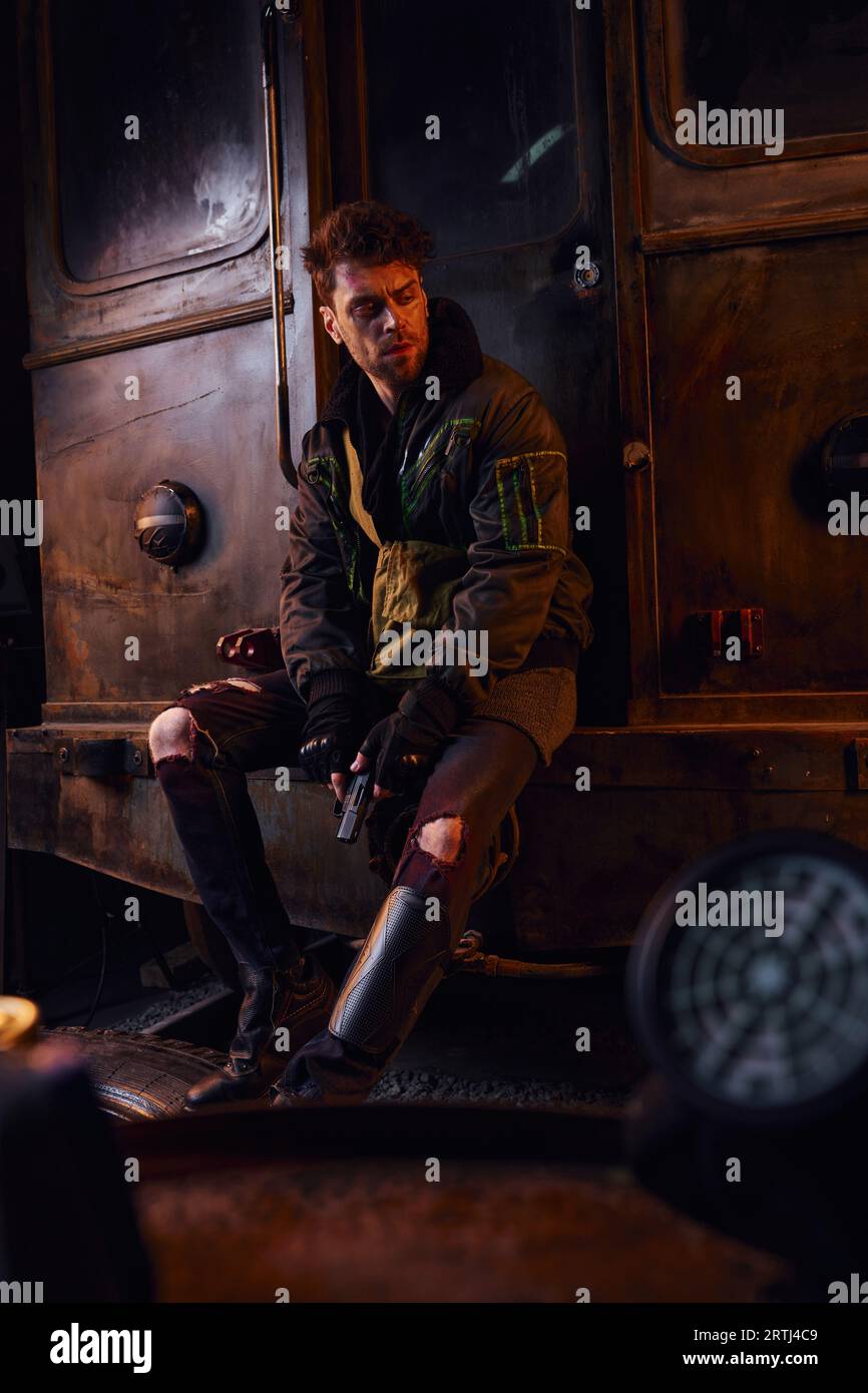 devastated man in worn clothes sitting with gun on rusty subway ...