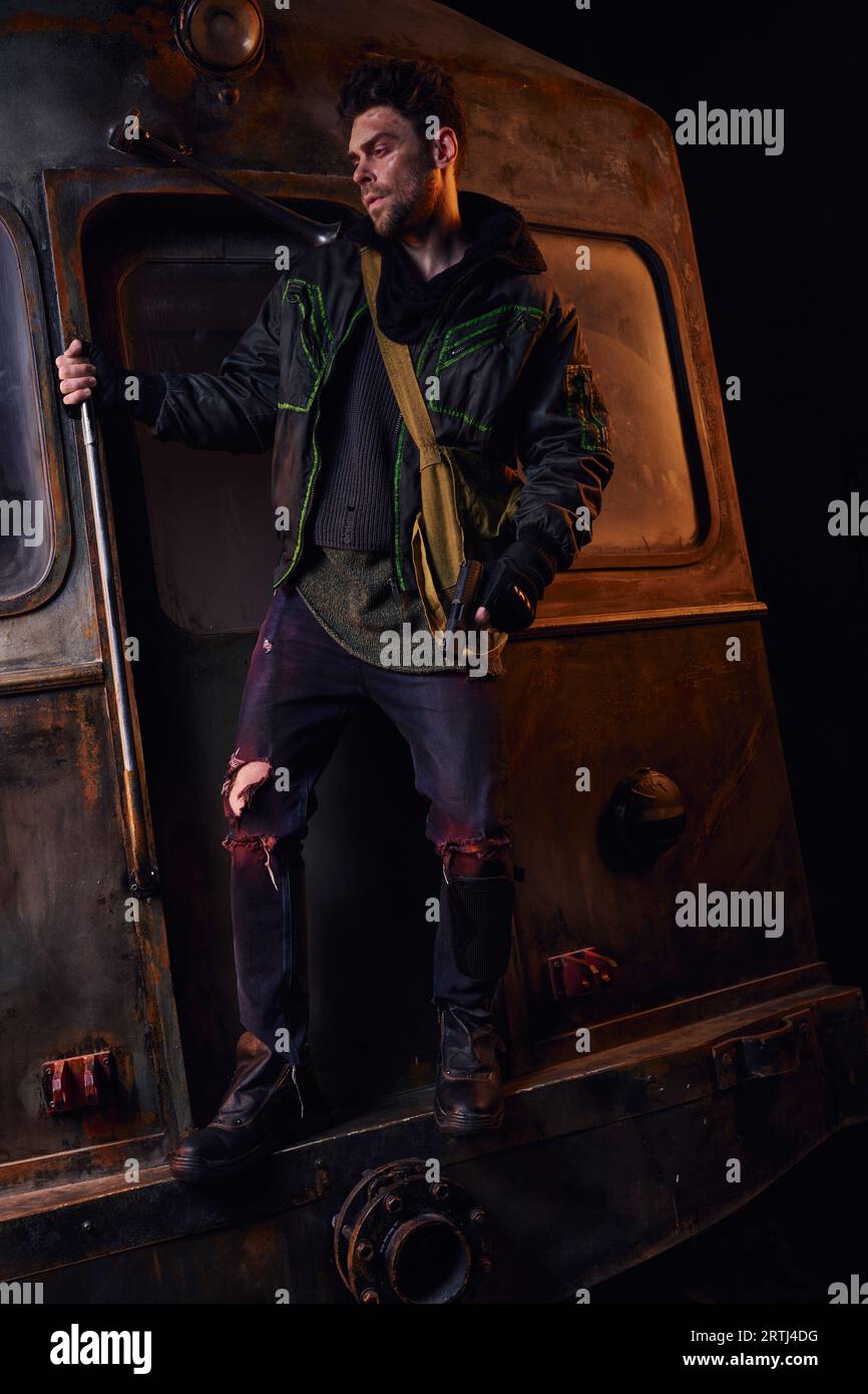 man in worn clothes standing with gun on rusty carriage in dark subway ...