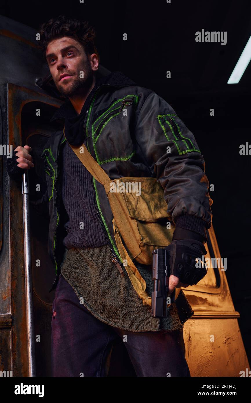 unshaven man with scratched face standing with canvas bag and gun in ...