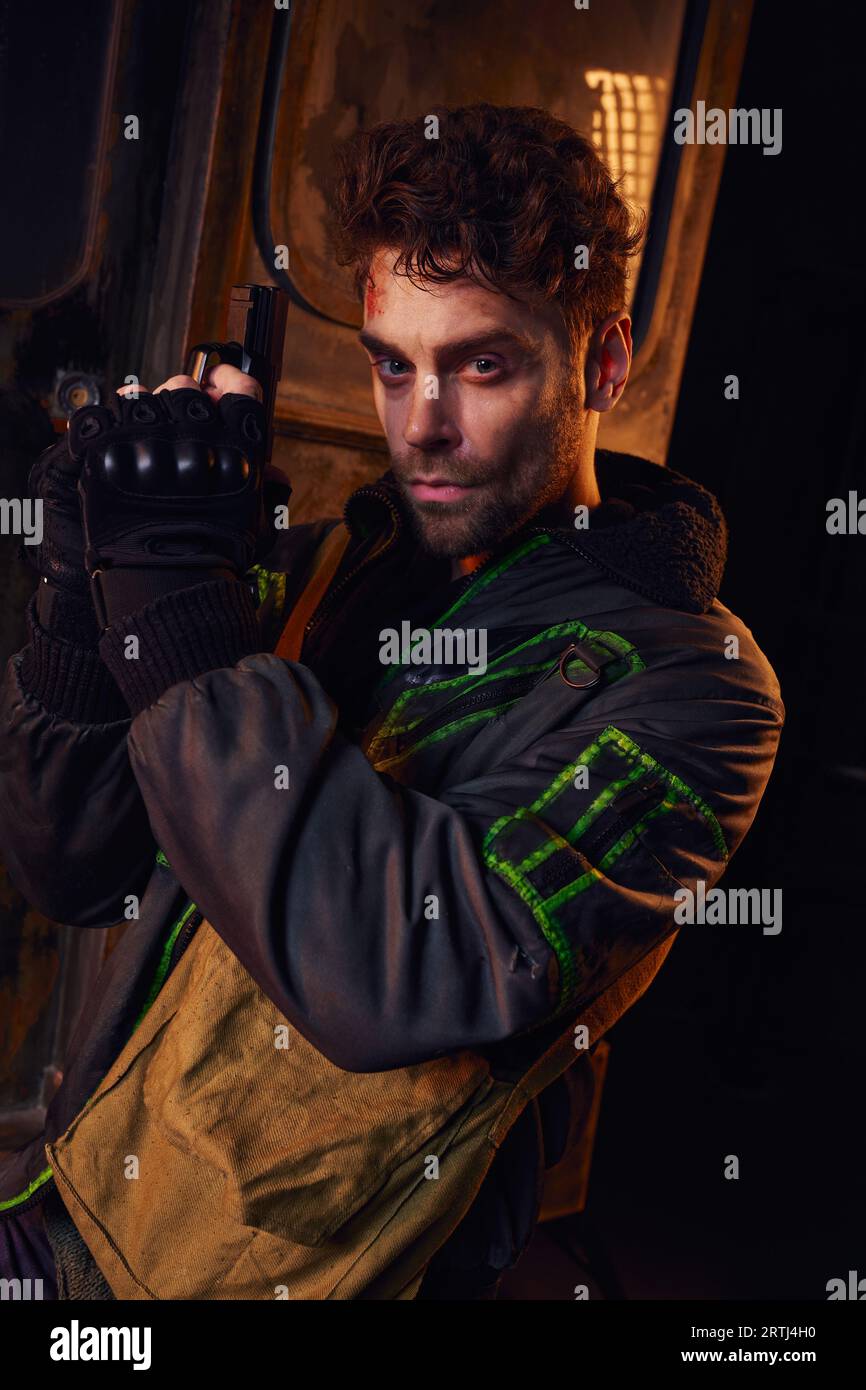 man with injured unshaven face and gun looking at camera in dark subway ...