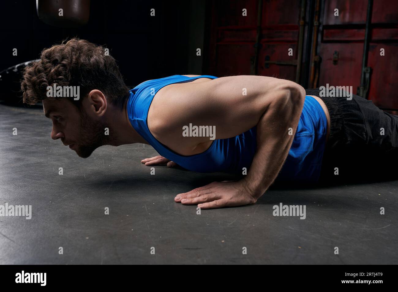 side view of sportive unshaven man doing push-ups on urban street at ...