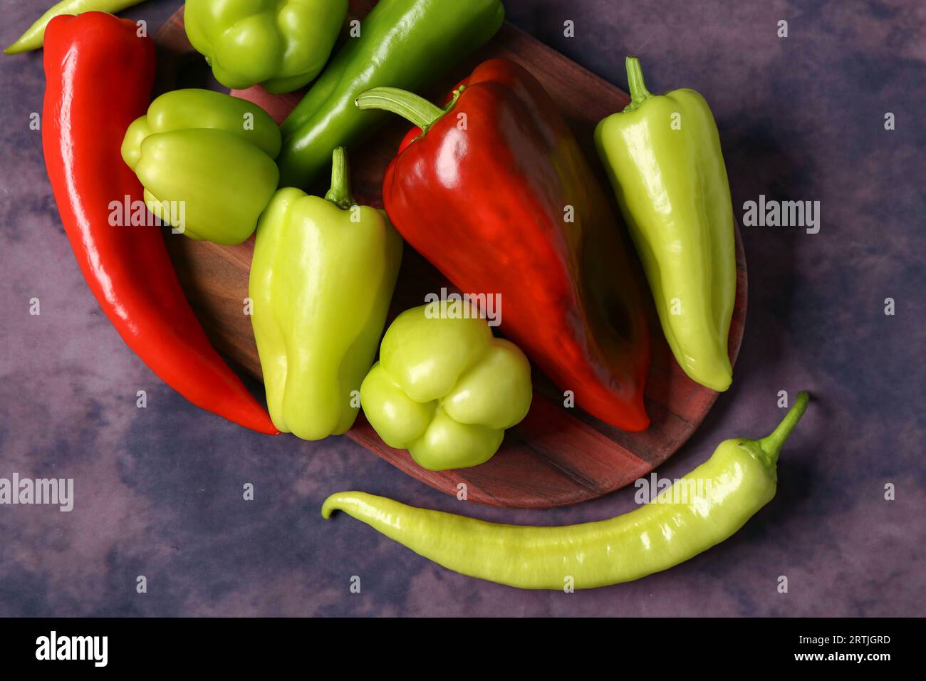 Wooden board with different fresh peppers on purple background Stock ...