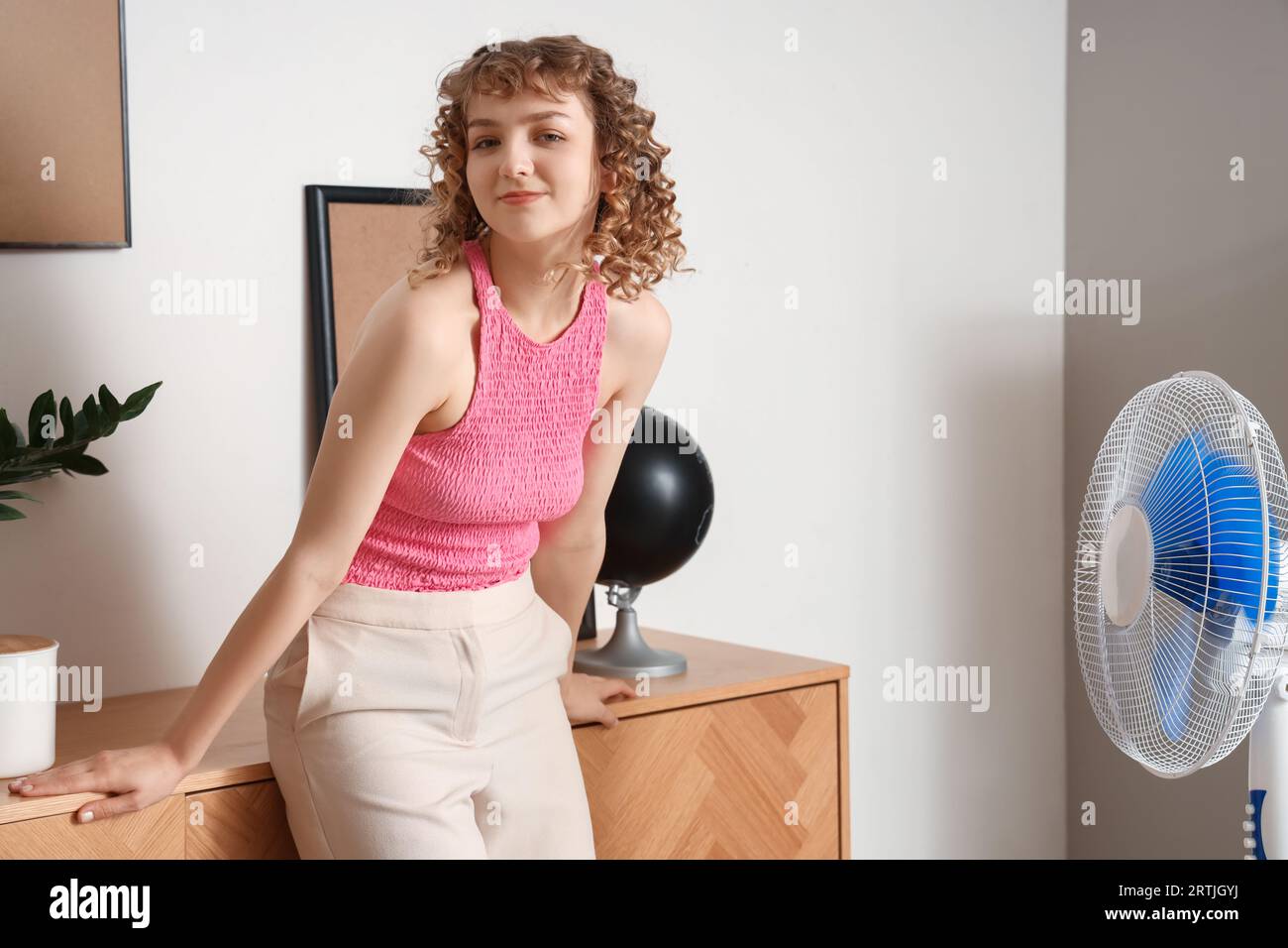 Beautiful happy young woman with electric fan in living room at home ...