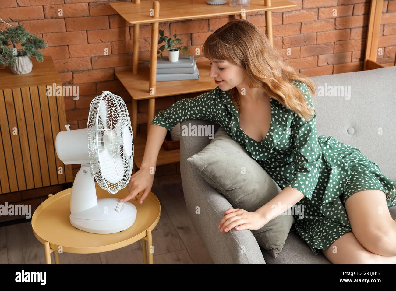Young woman with blowing electric fan sitting on sofa at home Stock ...