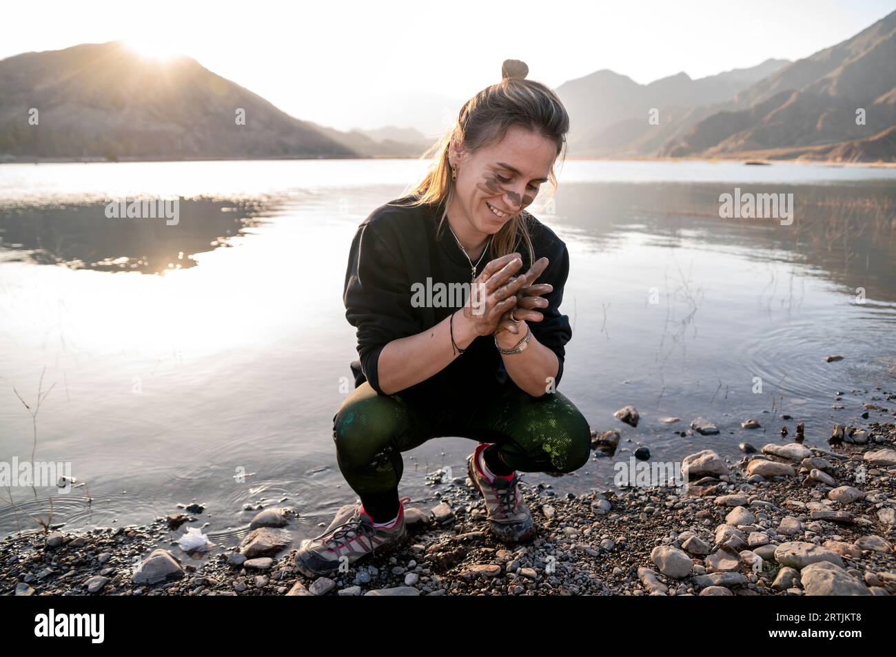 Woman putting mud on hands and face while enjoying outdoors in nature ...