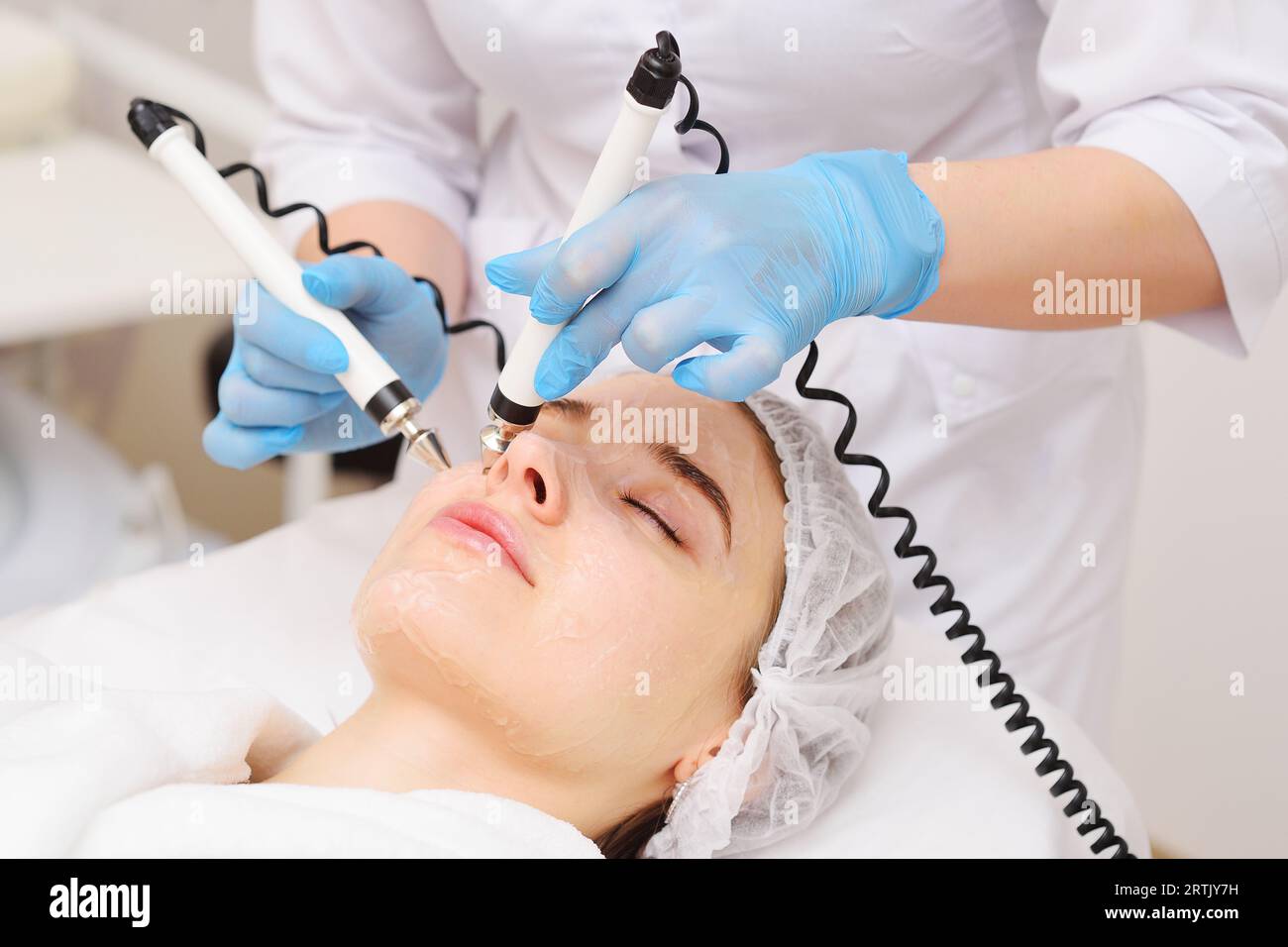 cosmetologist conducts microcurrent facial therapy for a young woman using a device in a beauty ...