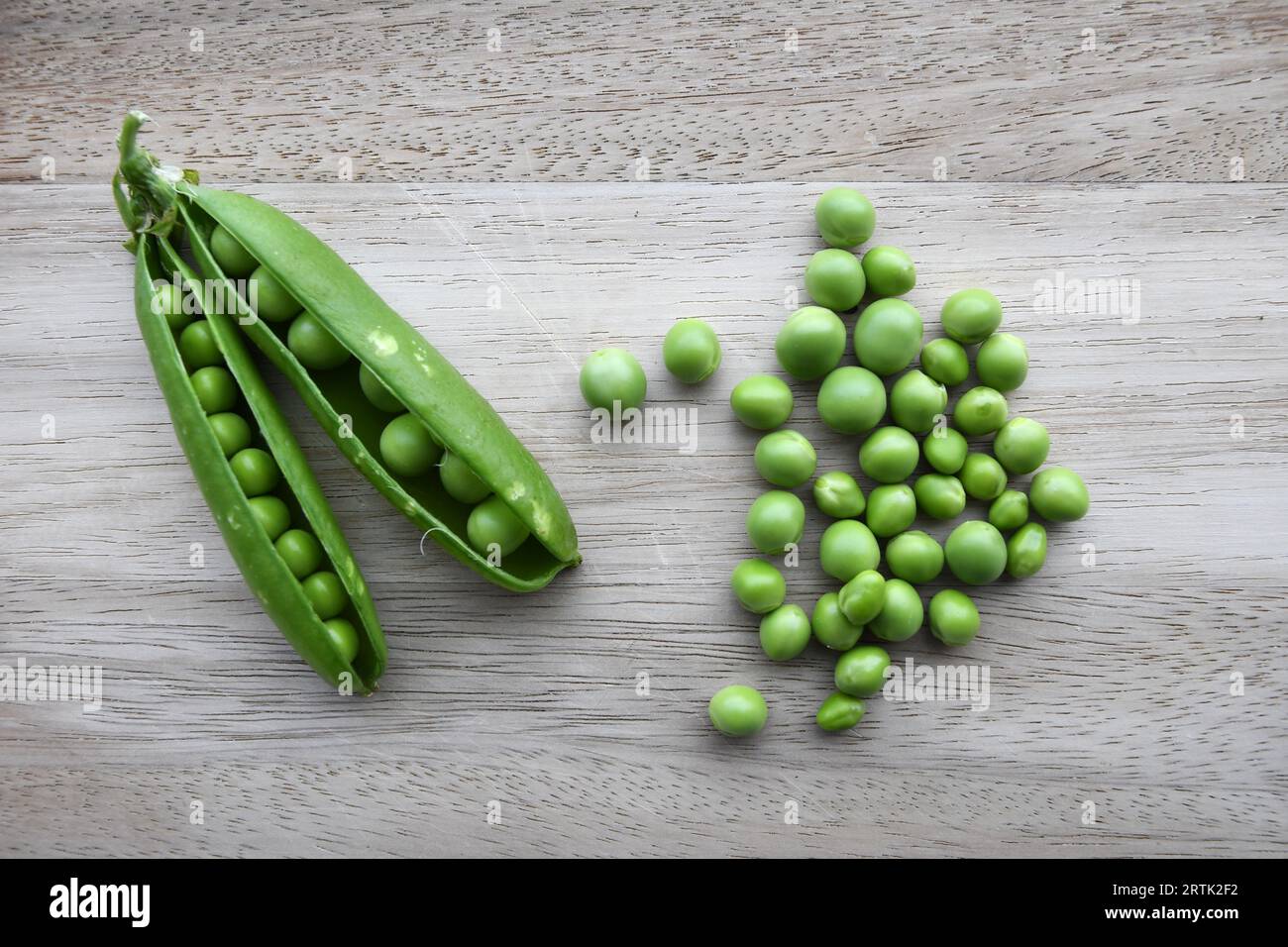 Garden peas (Pisum sativum) and two open pea pods isolated on a wood ...