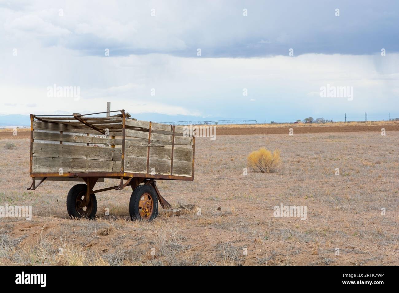 Weathered farm wagon on idle field in springtime with rain clouds above ...
