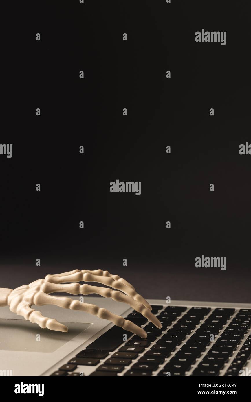 Vertical image of plastic skeleton hand on laptop keyboard with copy ...
