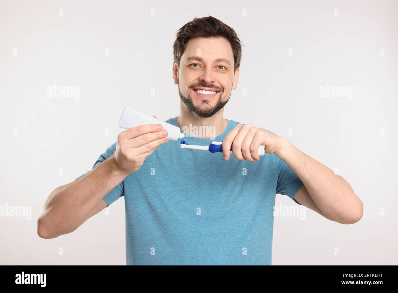 Happy man squeezing toothpaste from tube onto toothbrush on white ...