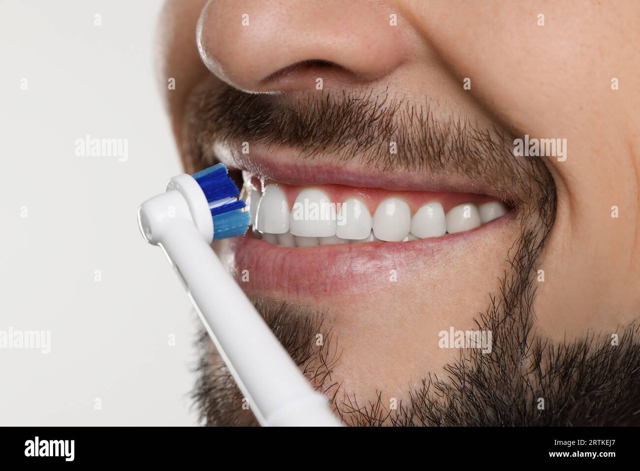 Man brushing his teeth with electric toothbrush on white background ...