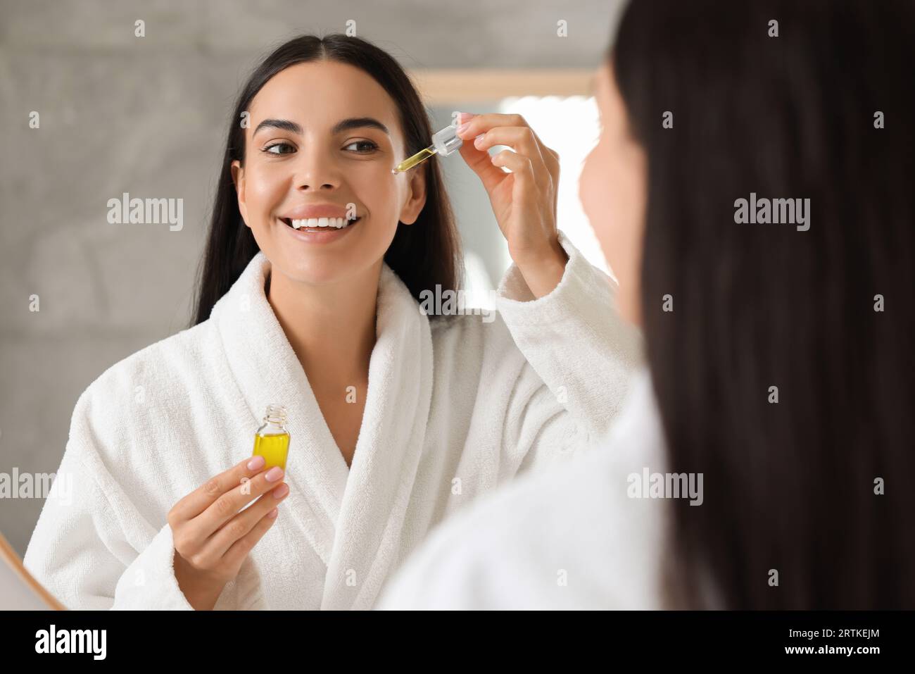 Beautiful young woman applying serum onto her face indoors Stock Photo ...