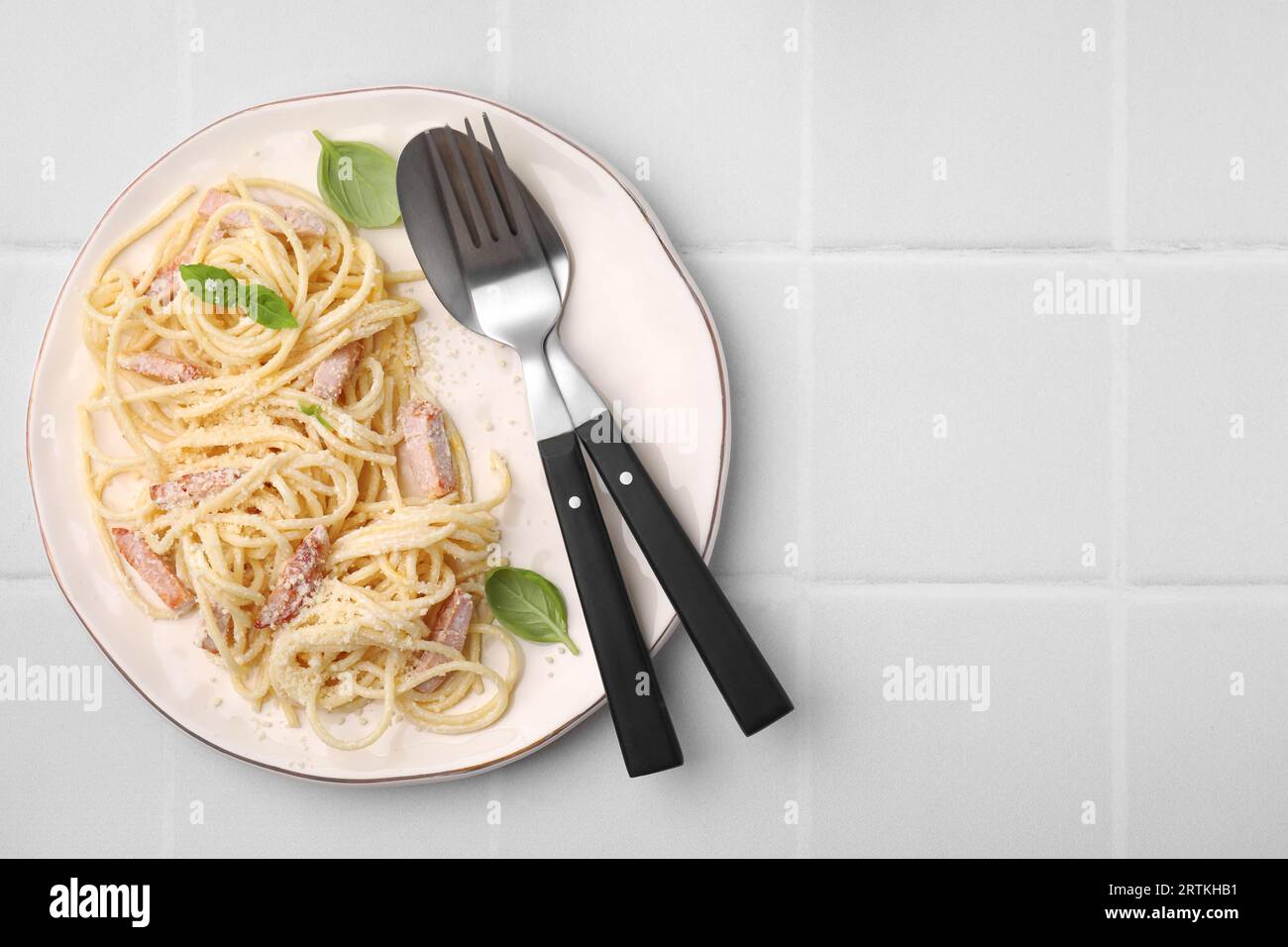 Plate of tasty pasta Carbonara with basil leaves on white tiled table ...